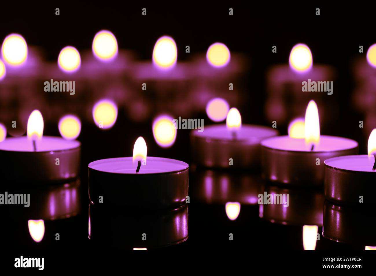 Burning violet candle on black background, closeup. Funeral attributes ...