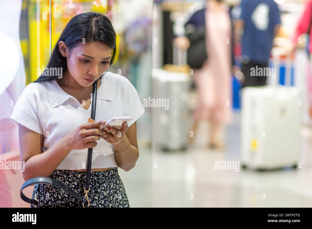A young woman uses a mobile phone at a shop window in a busy place ...