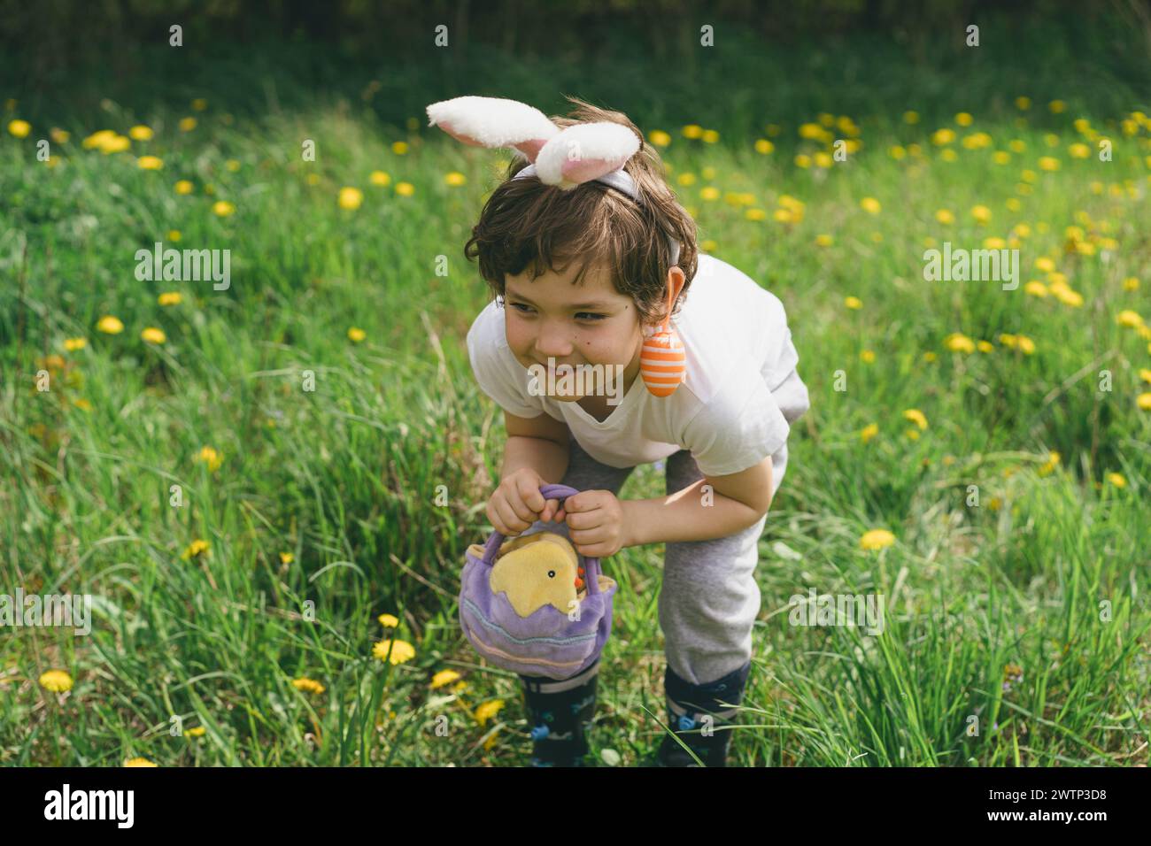 Boy with eggs basket and bunny ears on Easter egg hunt in sunny spring ...