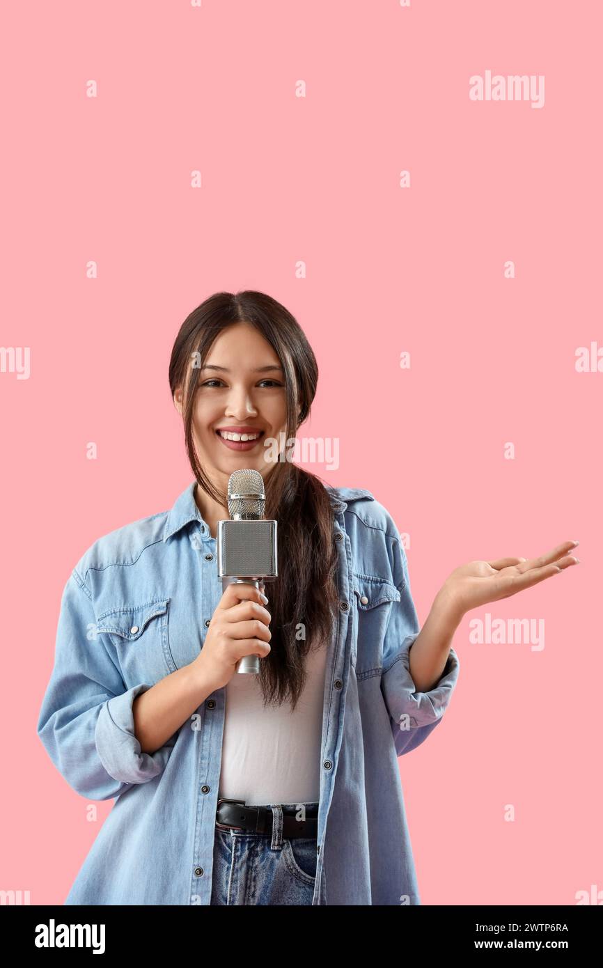 Female Asian journalist with microphone talking on pink background ...