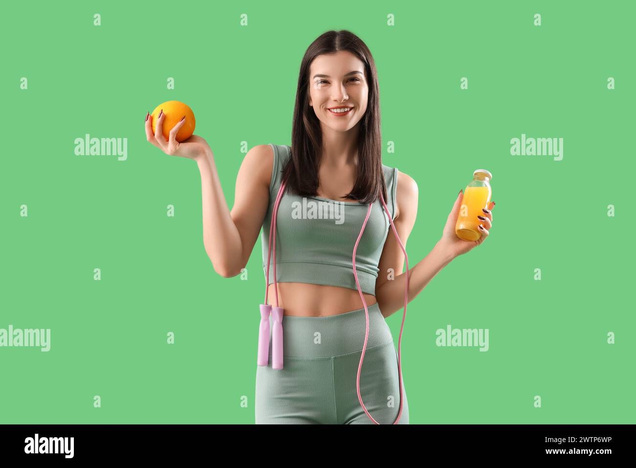 Sporty young woman with skipping rope and orange juice on green ...