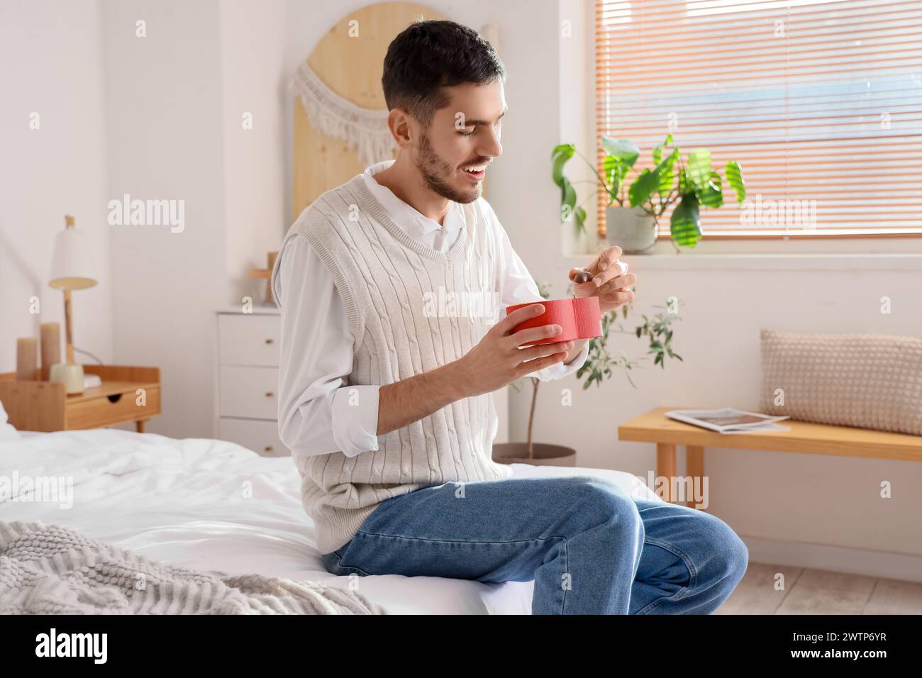 Handsome man with box of heart-shaped chocolate candies in bedroom ...