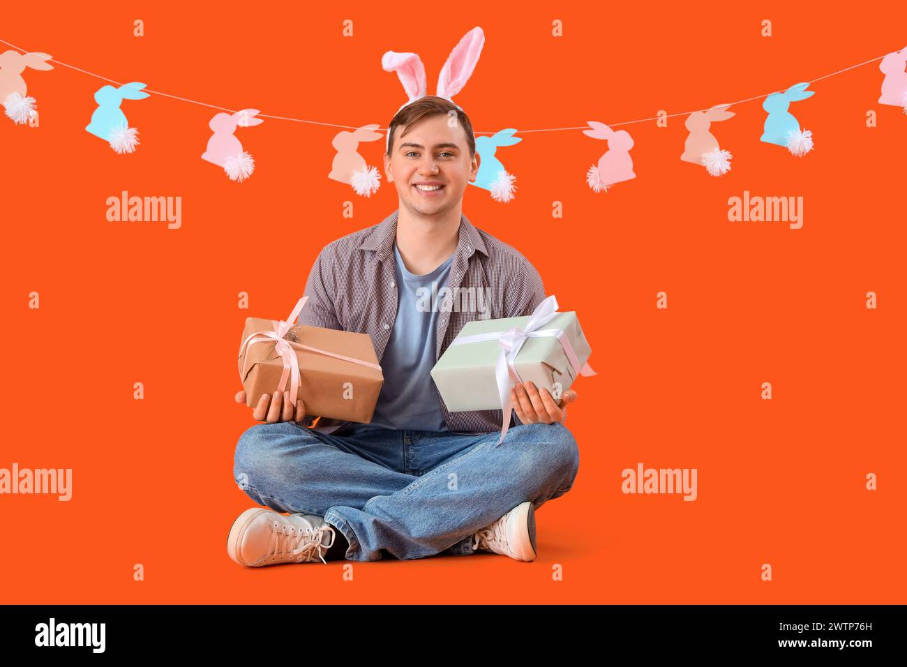 Happy young man in bunny ears with gift boxes and rabbits garland ...