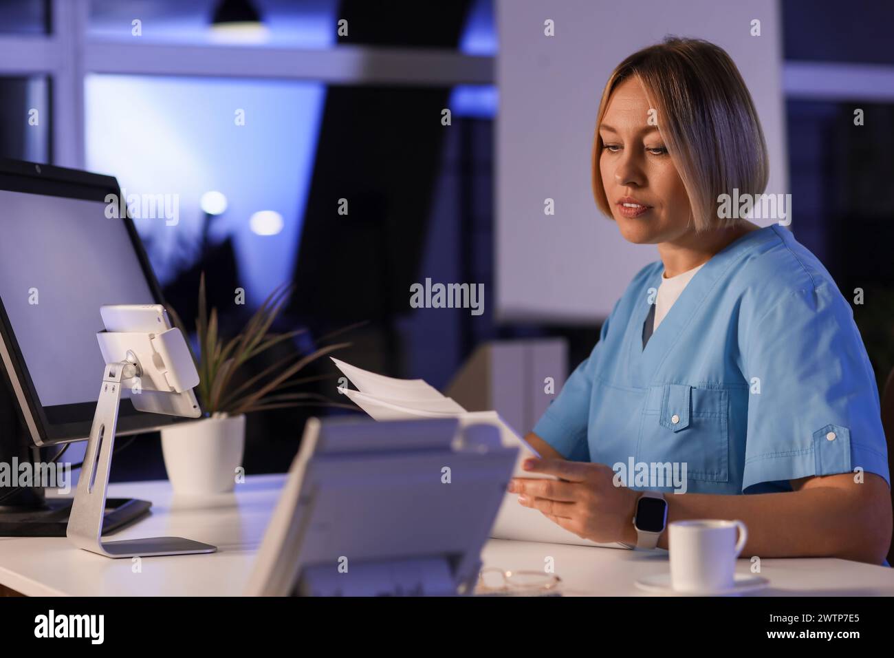 Female nurse with papers working evening shift at desk in clinic Stock ...