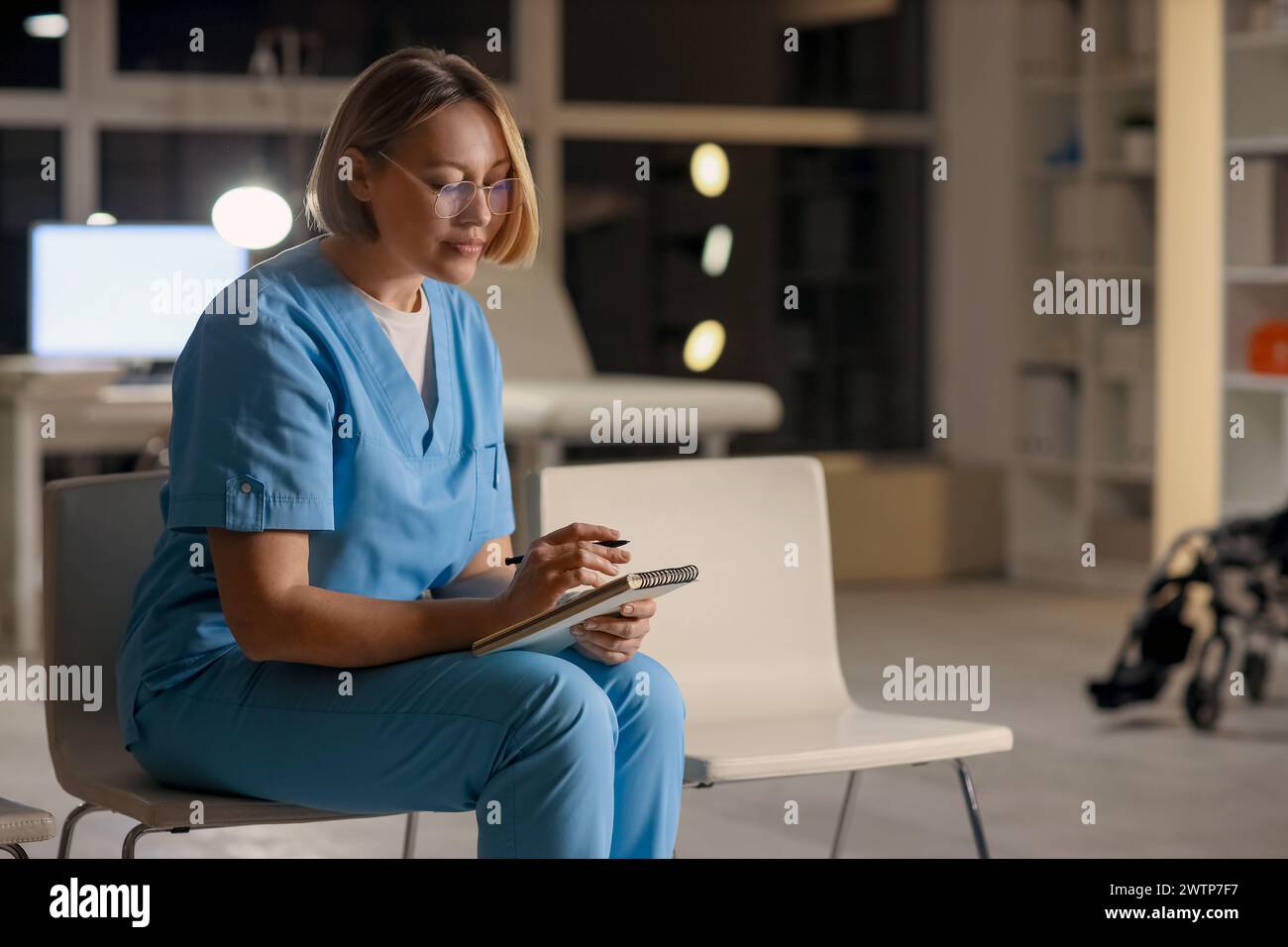 Female nurse with notebook sitting at hospital in evening Stock Photo ...