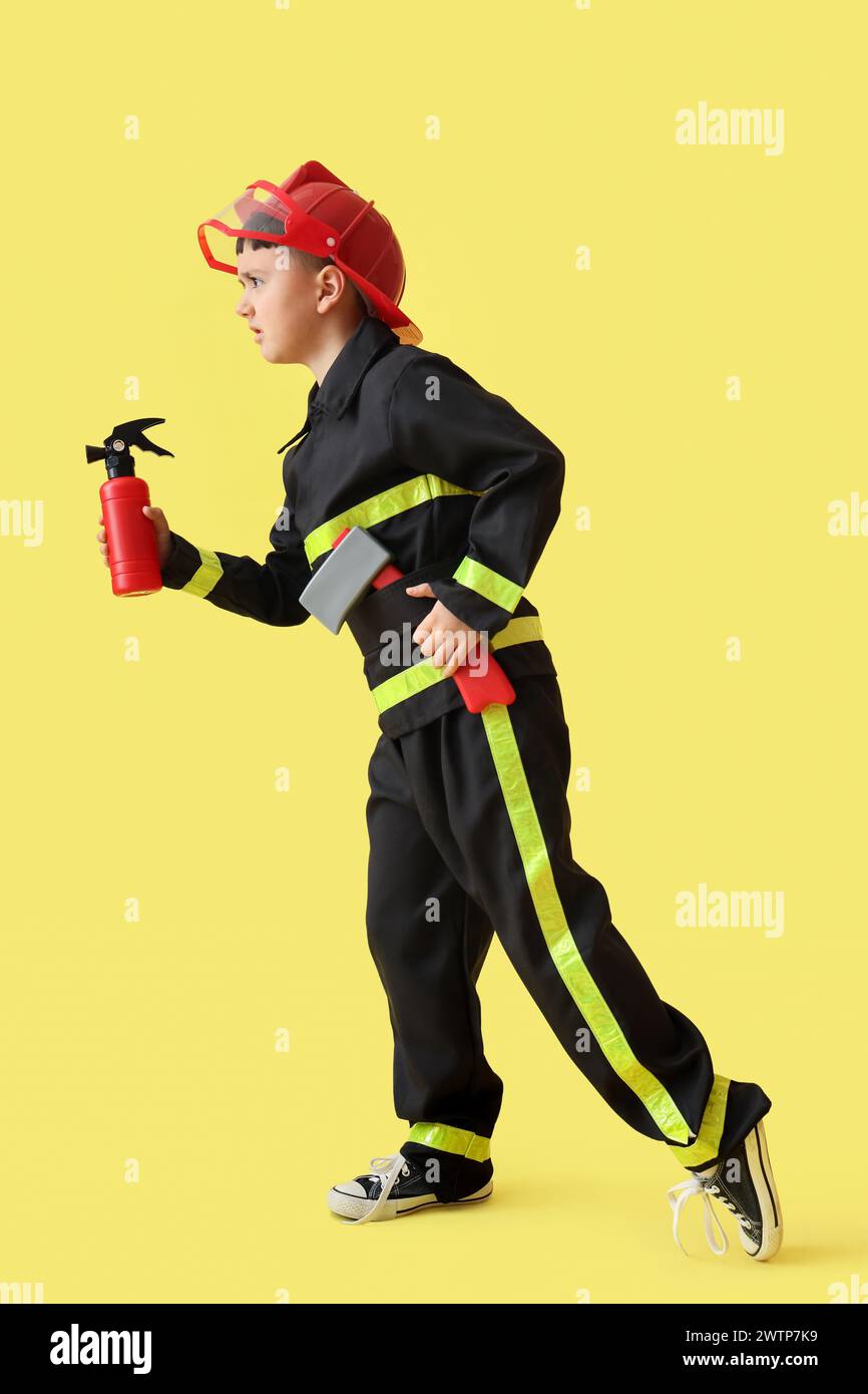 Cute little firefighter with toy tools running on yellow background ...
