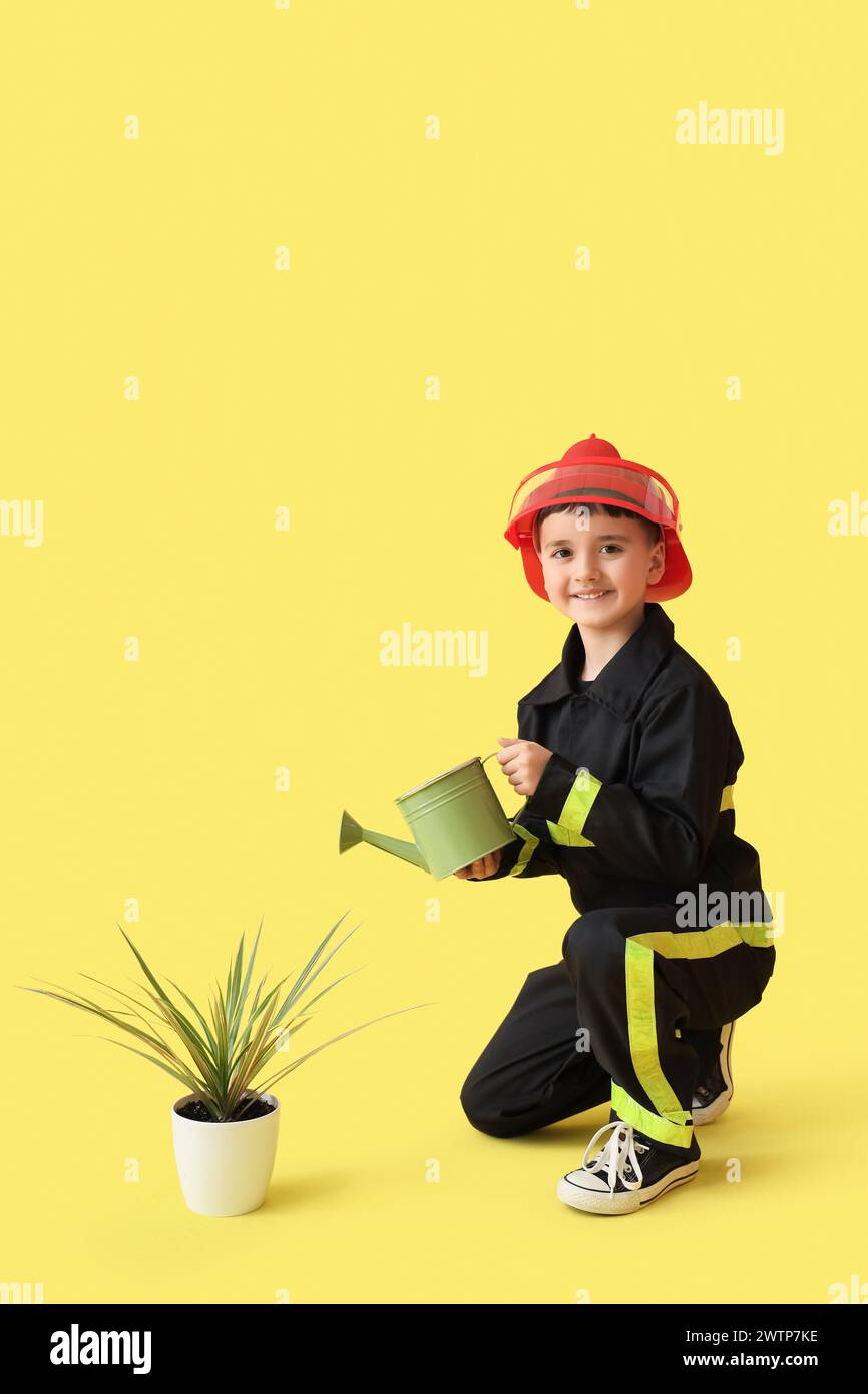 Cute little firefighter watering plant on yellow background Stock Photo ...