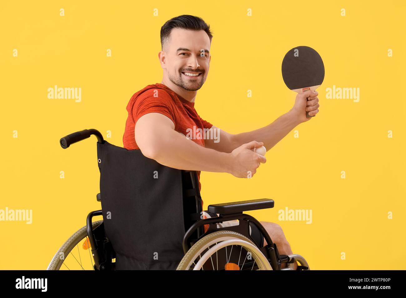 Sporty young man in wheelchair with ping pong racket and ball on yellow ...