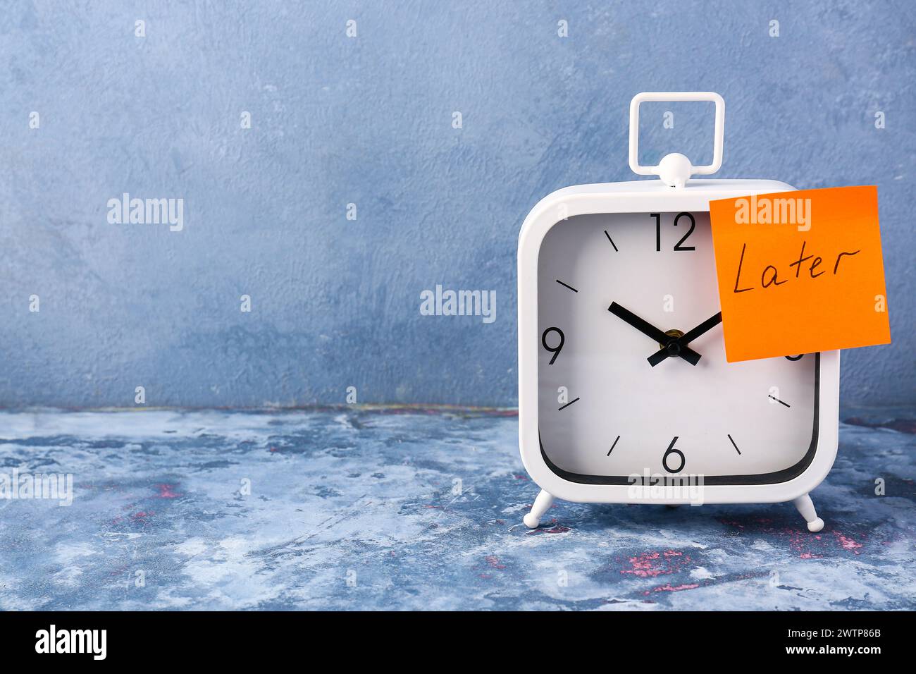 Text LATER with white alarm clock on table against blue background ...