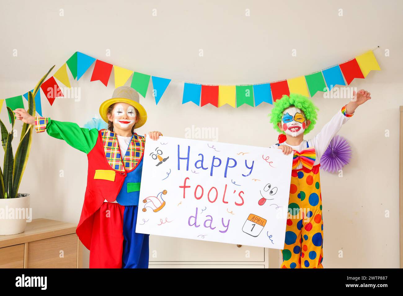 Funny little children in clown costumes with poster at home. April ...