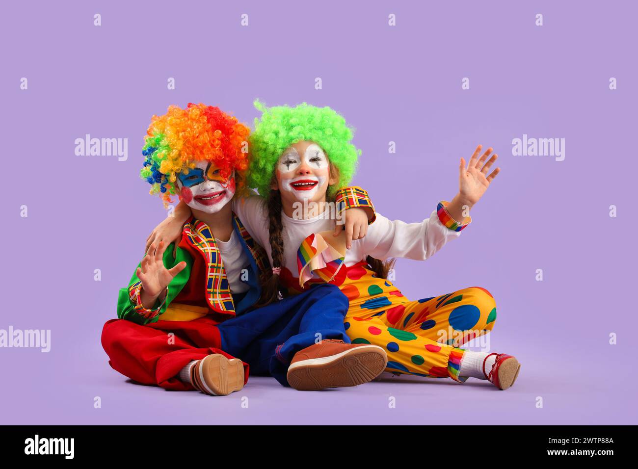 Funny little children in clown costumes hugging on lilac background ...