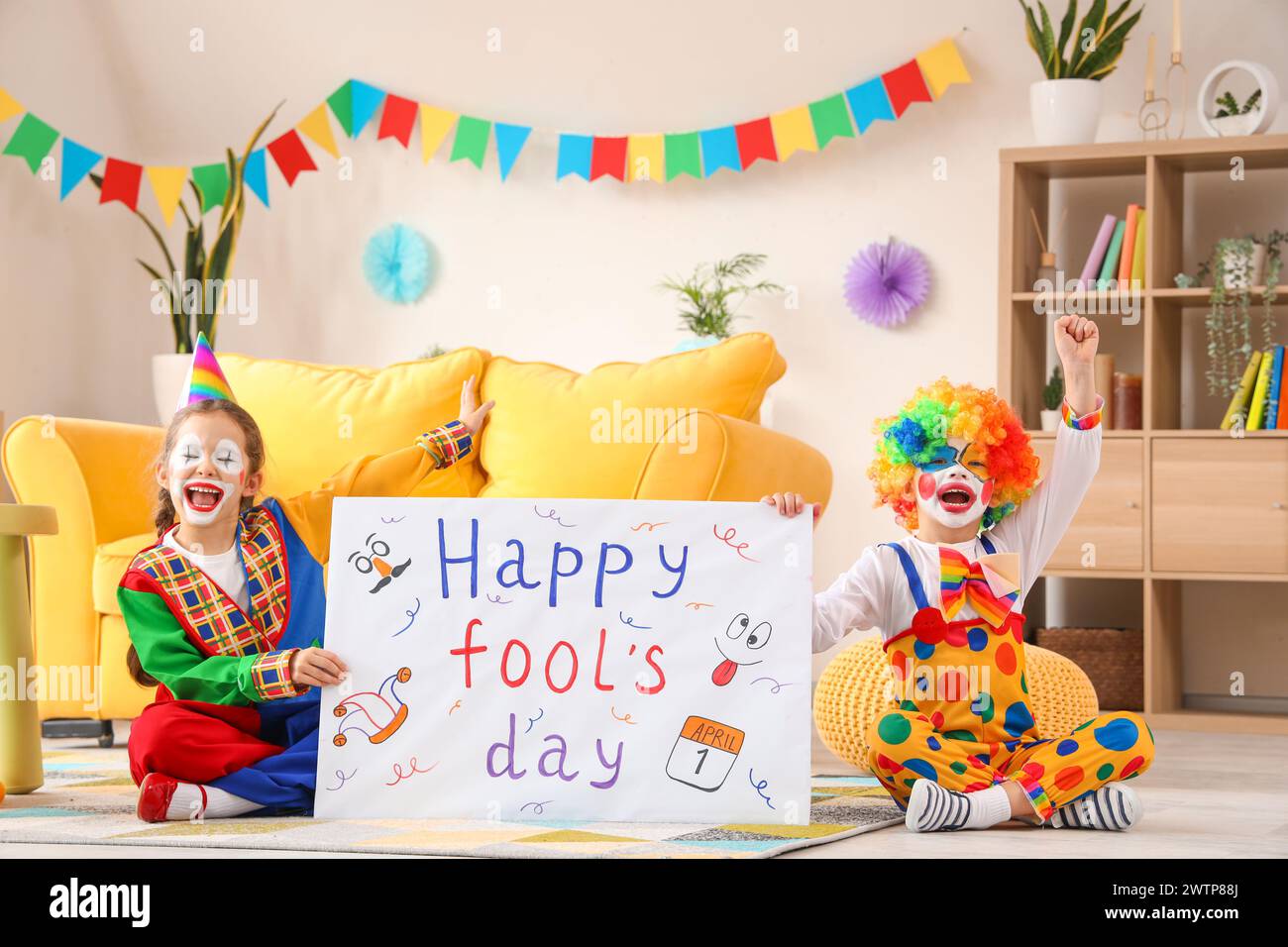 Funny little children in clown costumes with poster at home. April ...