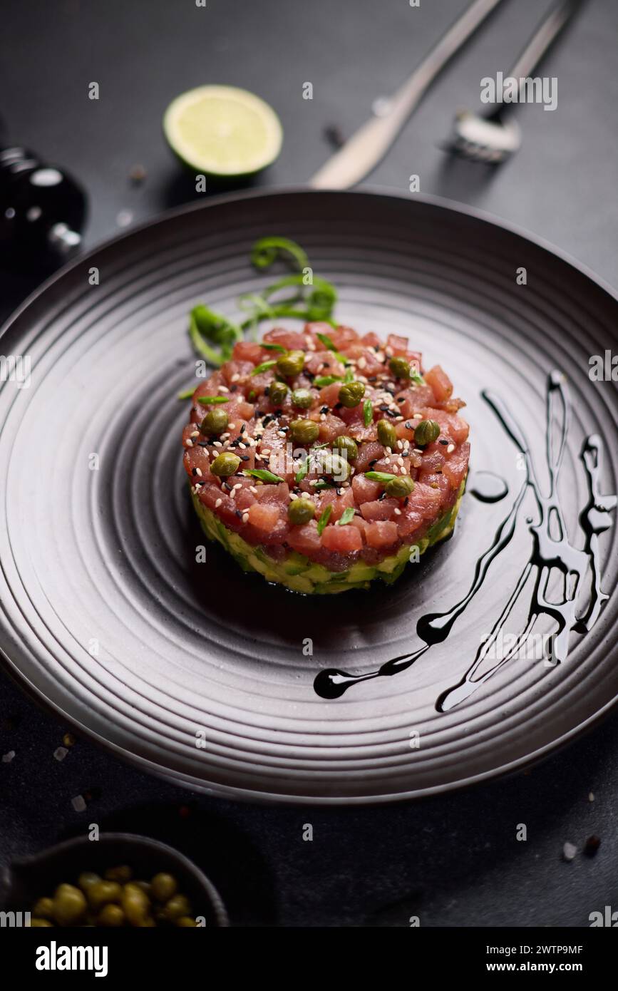 Tuna and avocado tartare with sesame seeds and capers on a dark ceramic ...