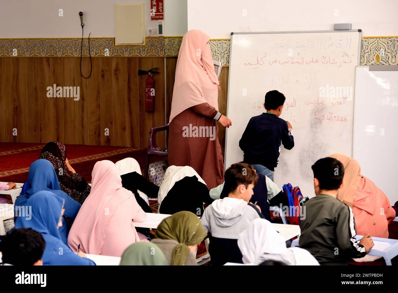An Arabic teacher wearing a veil reviews a student's writing in a ...