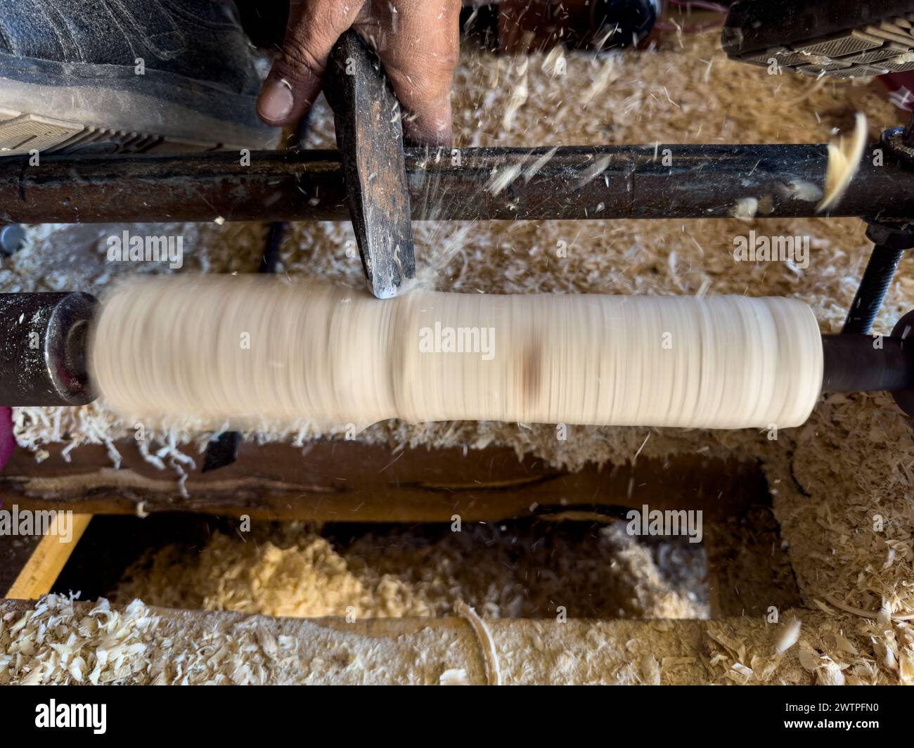 Carpenter shaping a piece of wood with wood turning and lathe flying ...