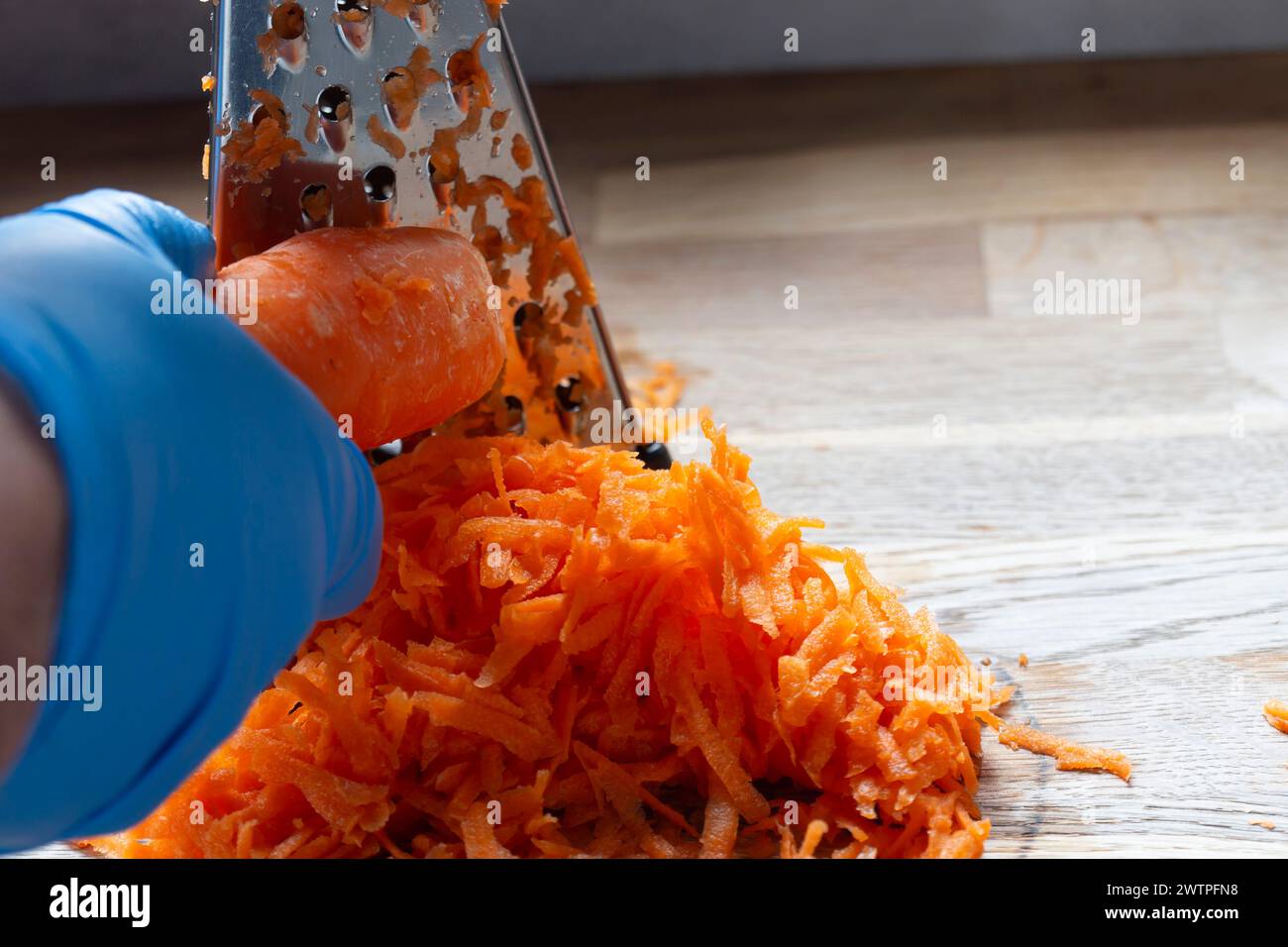 Person, wearing rubber gloves, grating fresh raw carrot with a metal ...