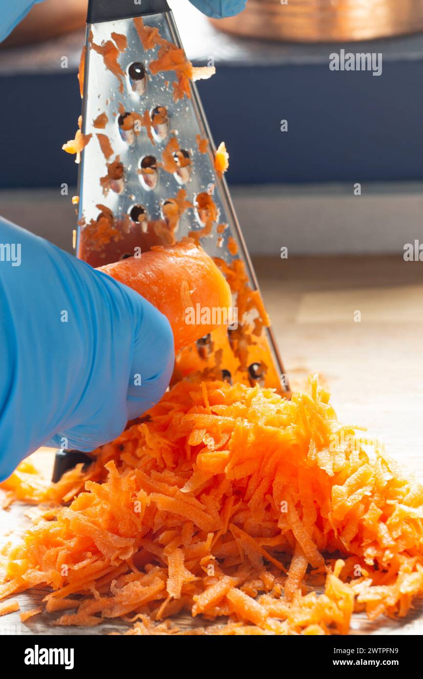 Person, wearing rubber gloves, grating fresh raw carrot with a metal ...