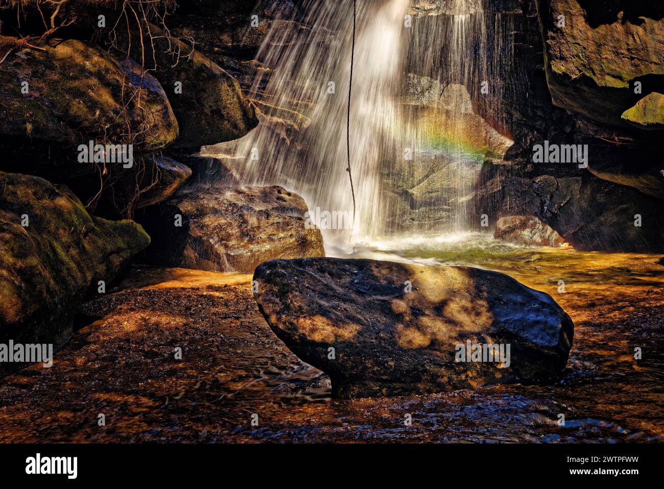 A nighttime waterfall cascades near rocks and trees, creating a rainbow ...