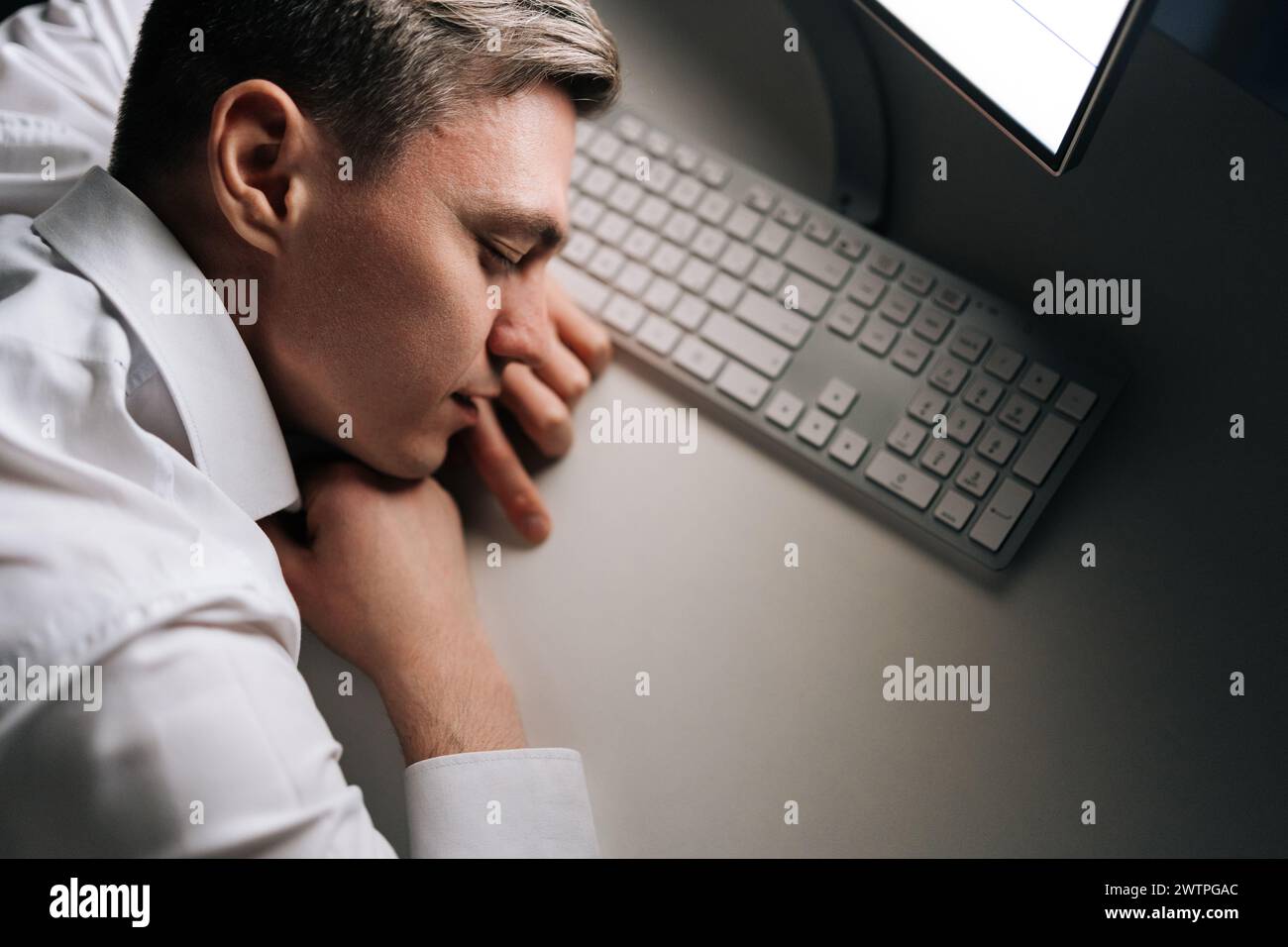 Top view of tired sleepy male employee asleep on computer desk late at ...