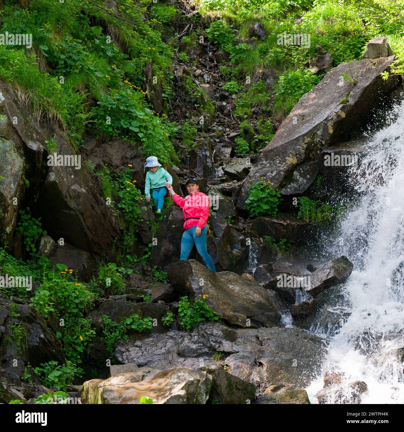 Mother and daughter are standing near a mountain waterfall, active ...