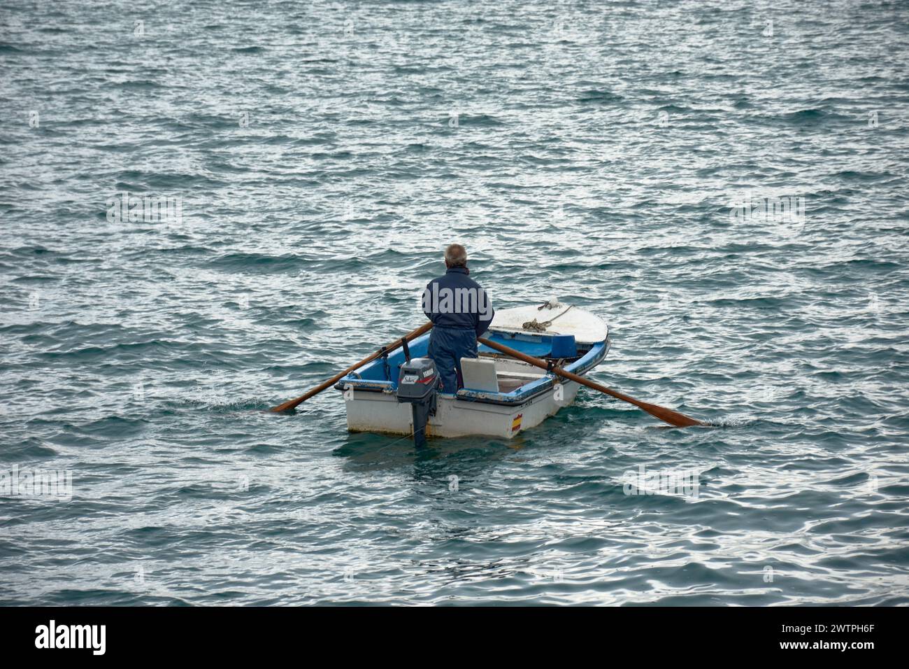 Fisherman with a rowboat and in blue overalls rows with his back to the ...