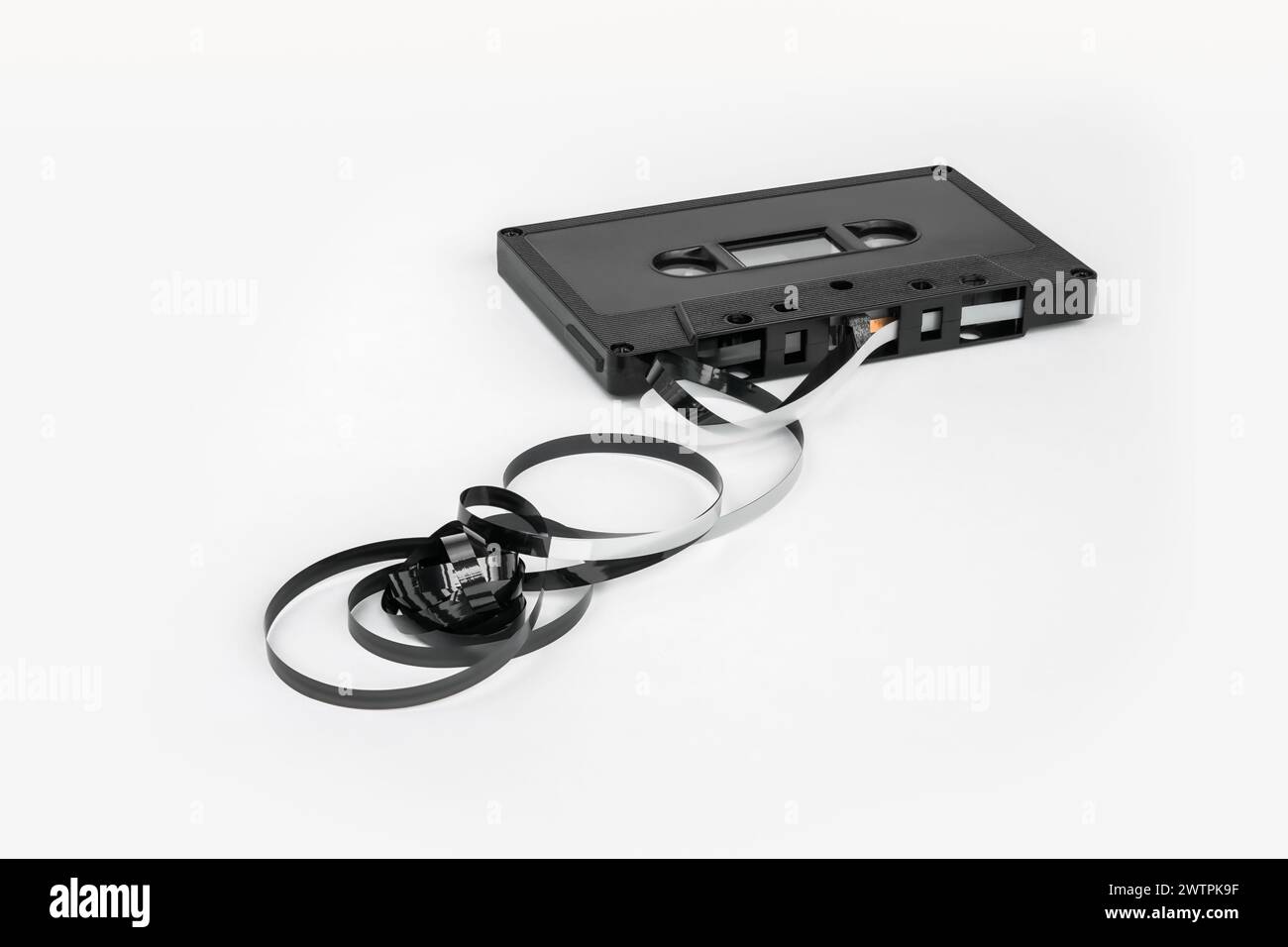 A black cassette tape lies on a white background with a tangled spiral ...