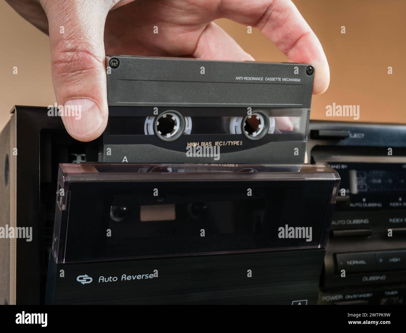 A man's hand holds an audio cassette over the open cassette deck of an ...