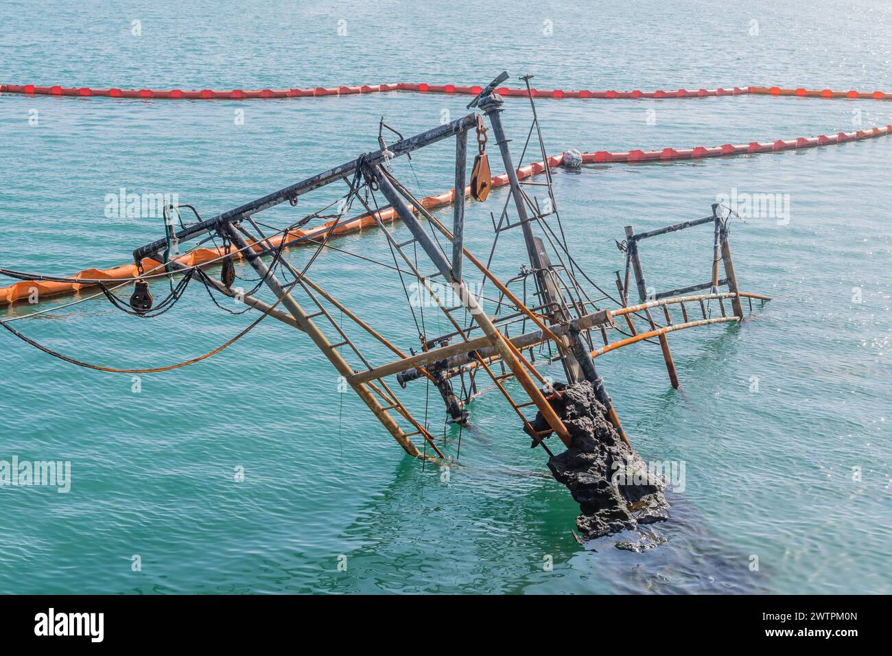 Rusty remnants of a sunken ship with booms and an orange barrier on ...