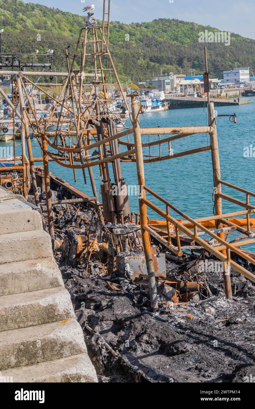 A burnt and rusty ship by the sea with boats in the background, in ...