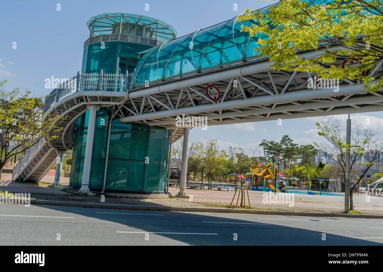 A modern elevated walkway beside a building with green trees and blue ...