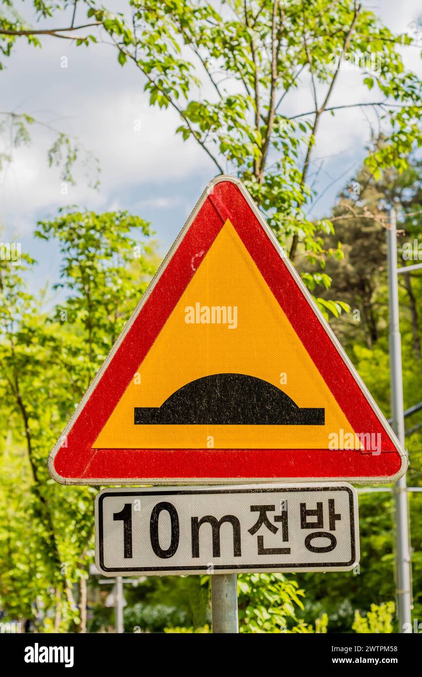 A traffic sign warning of a speed bump ahead with Korean text beneath ...