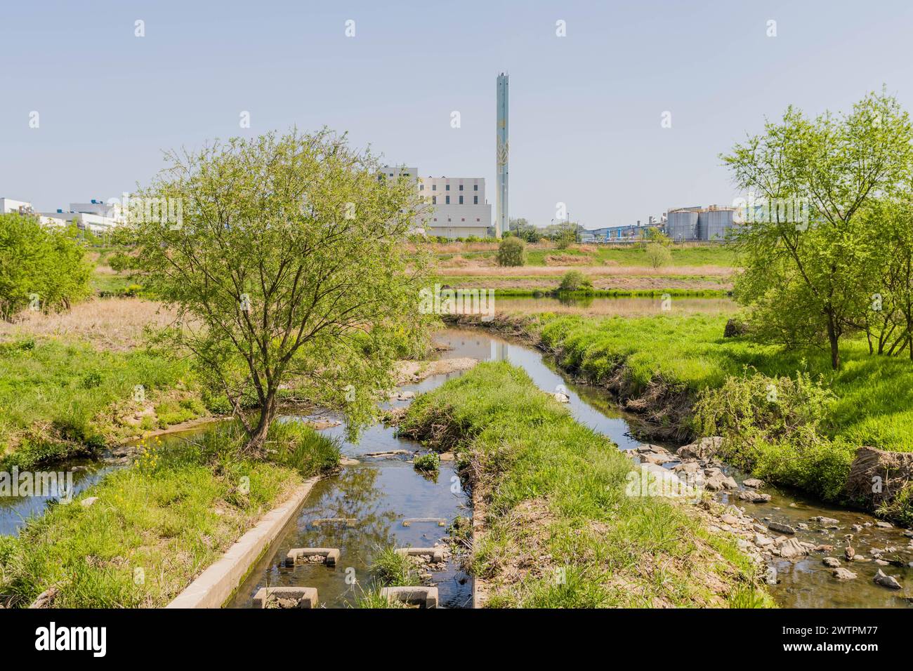A view of a stream meandering past industrial buildings with a tall ...