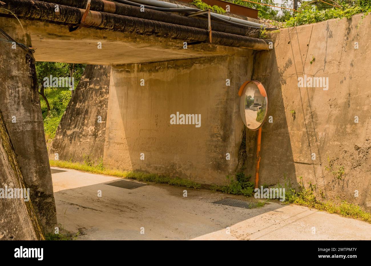 Shadowy underpass framing a traffic mirror and an orange cone on the ...
