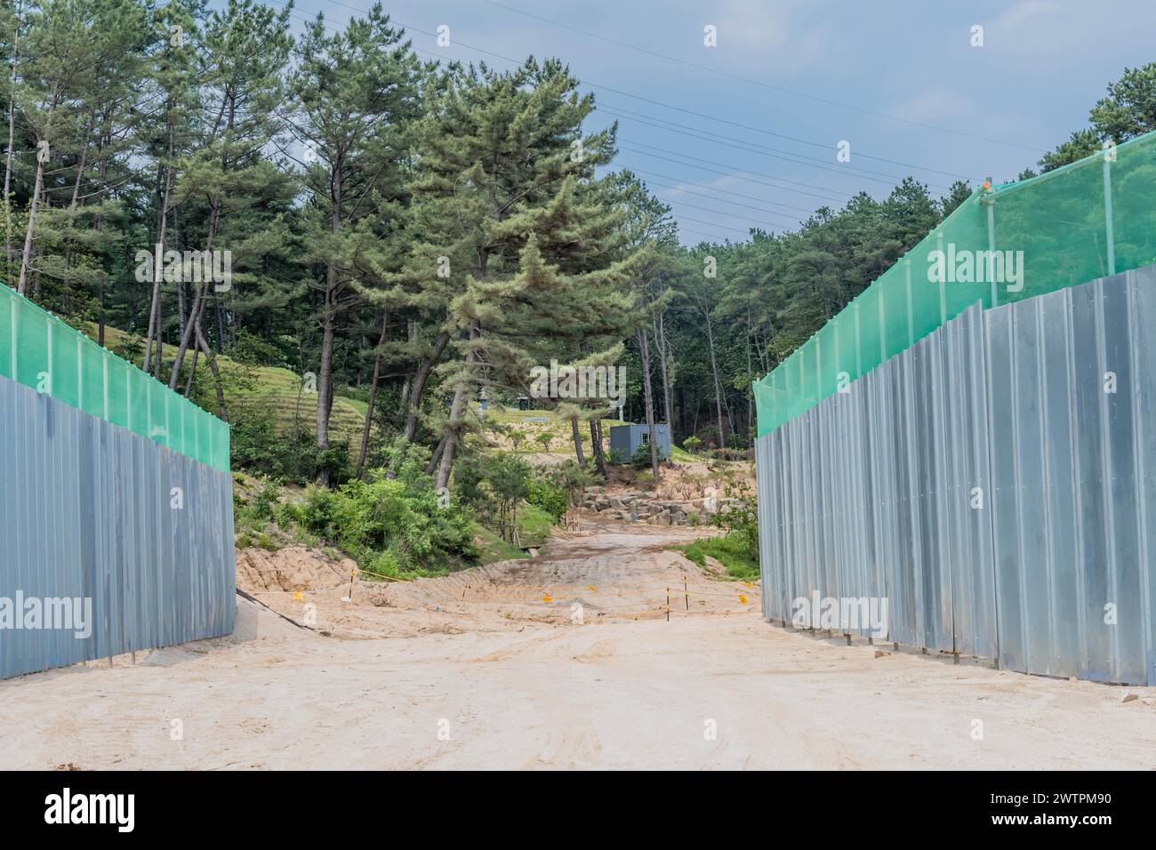 Entrance to a construction area with metal barricades and green netting ...