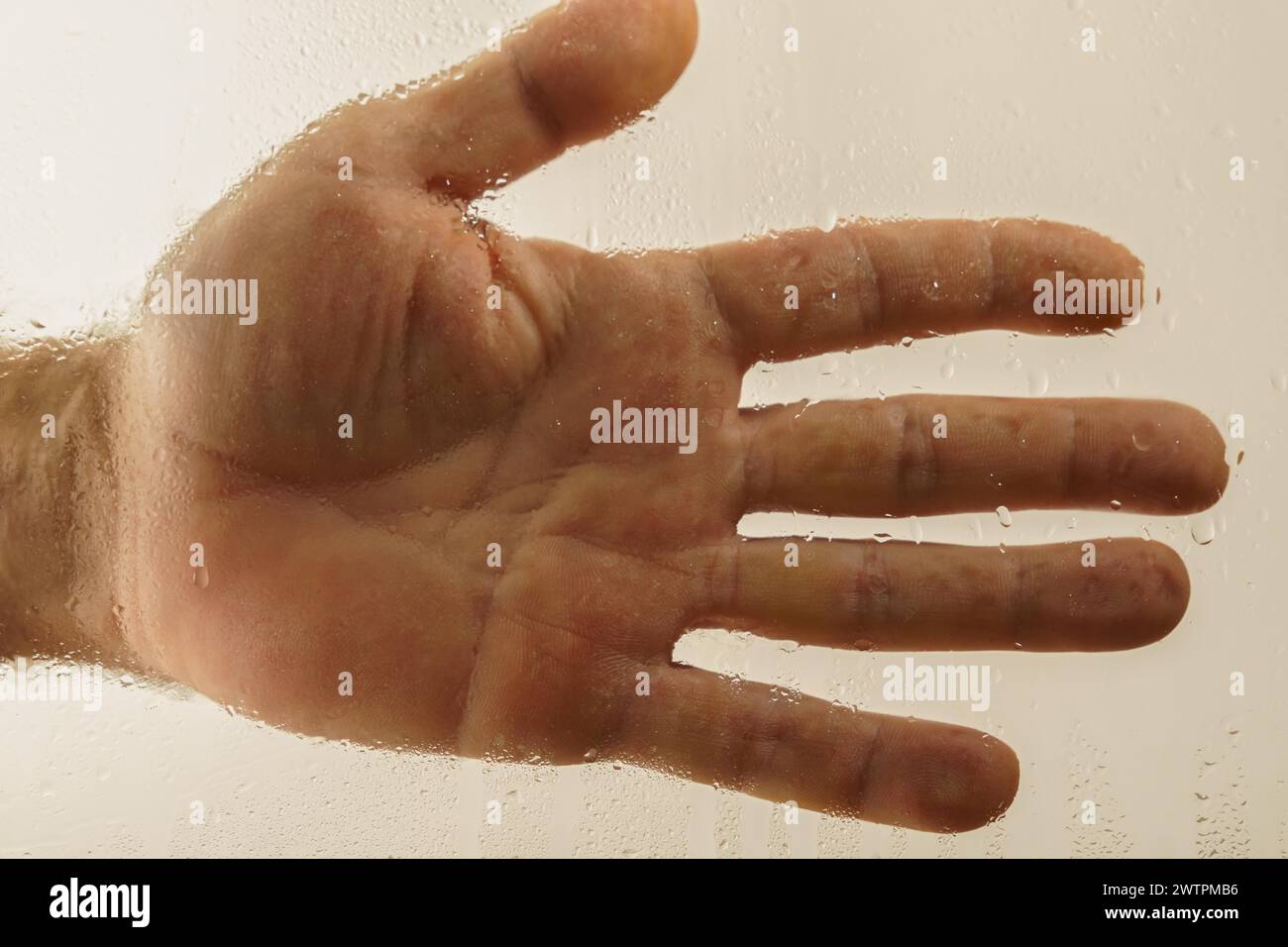 A man's hand on a rain-soaked window pane against a white background ...