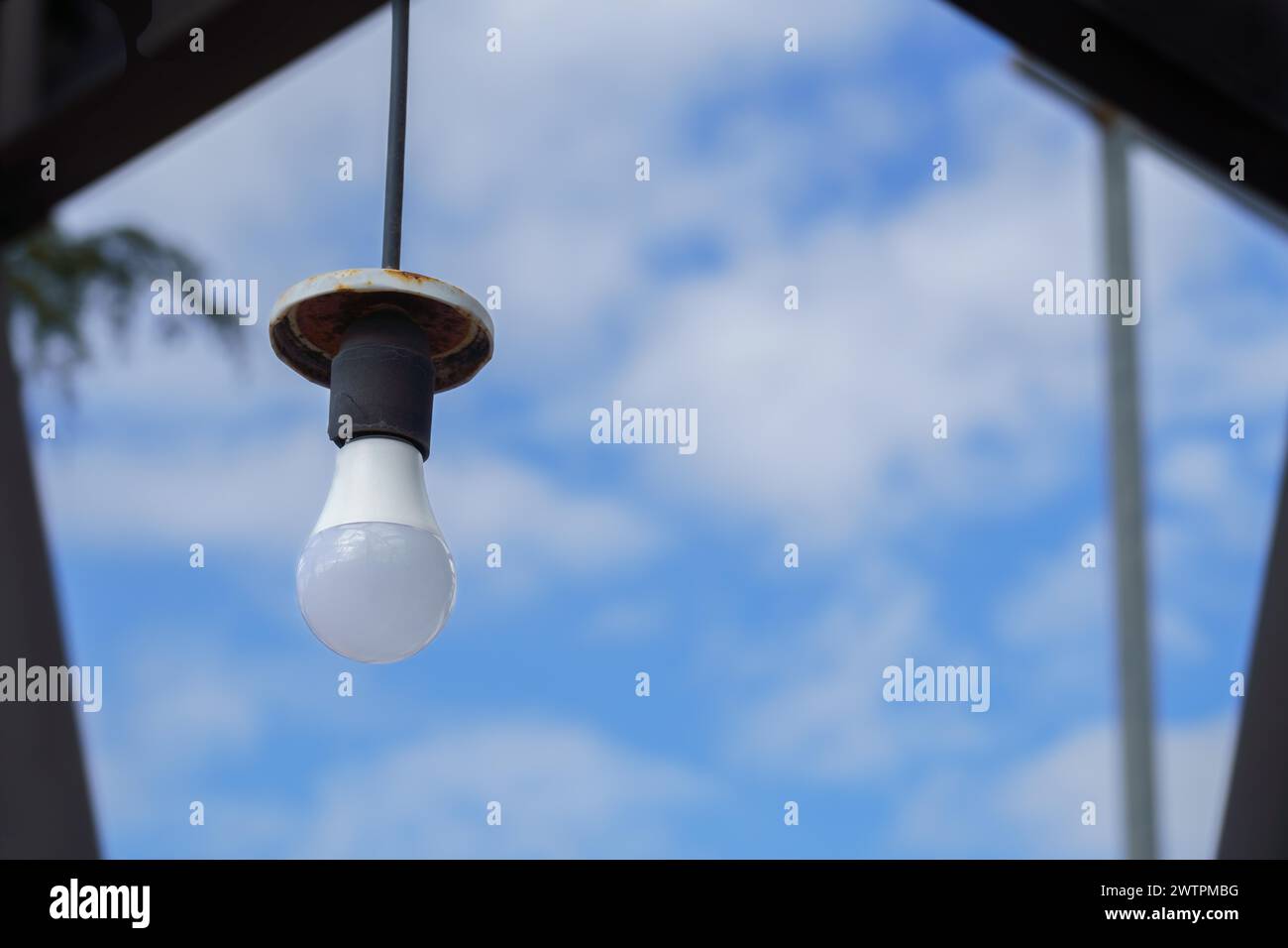 Light bulb hanging from a wire with a rusty lamp over a blue sky with ...