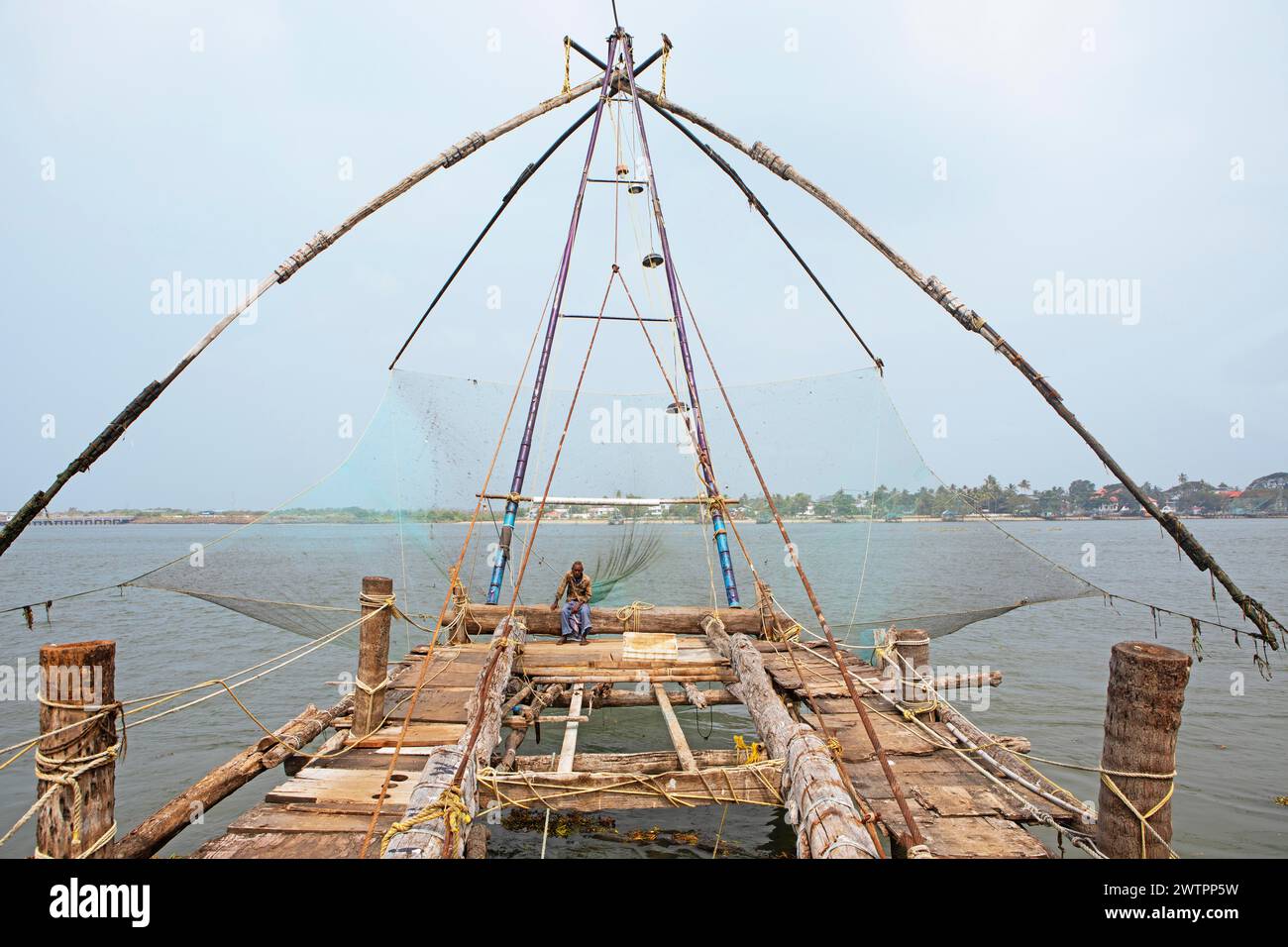 Indian fisherman sitting on a Chinese fishing net, behind him the ...