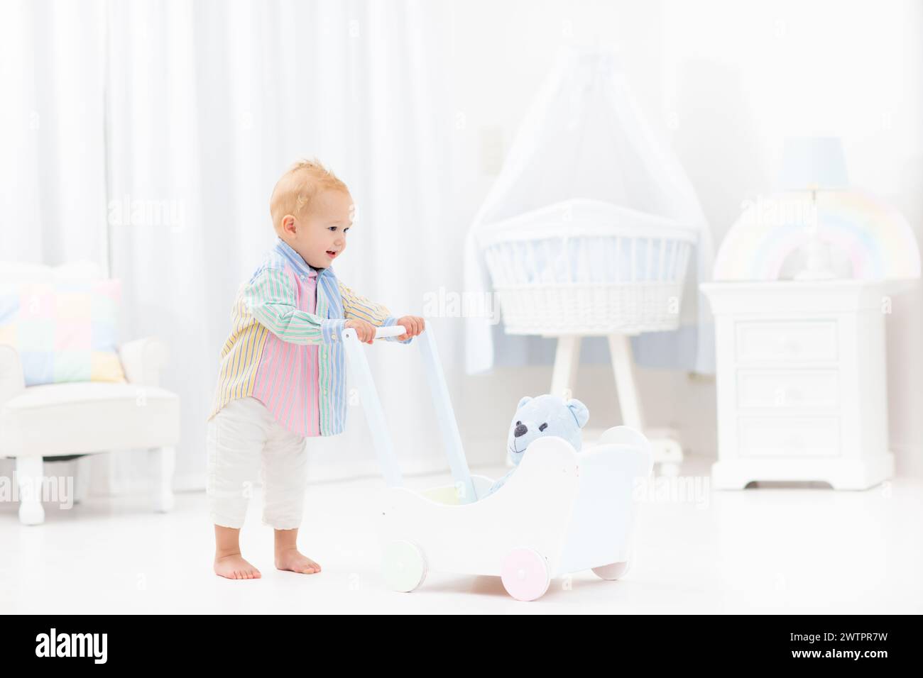 Baby boy learning to walk with wooden push walker in white bedroom with ...