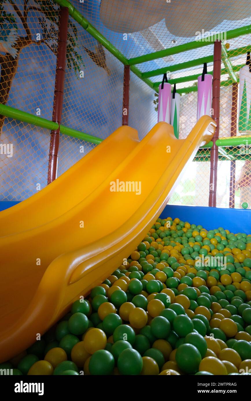 Yellow slide at indoor playground against colourful plastic balls ...
