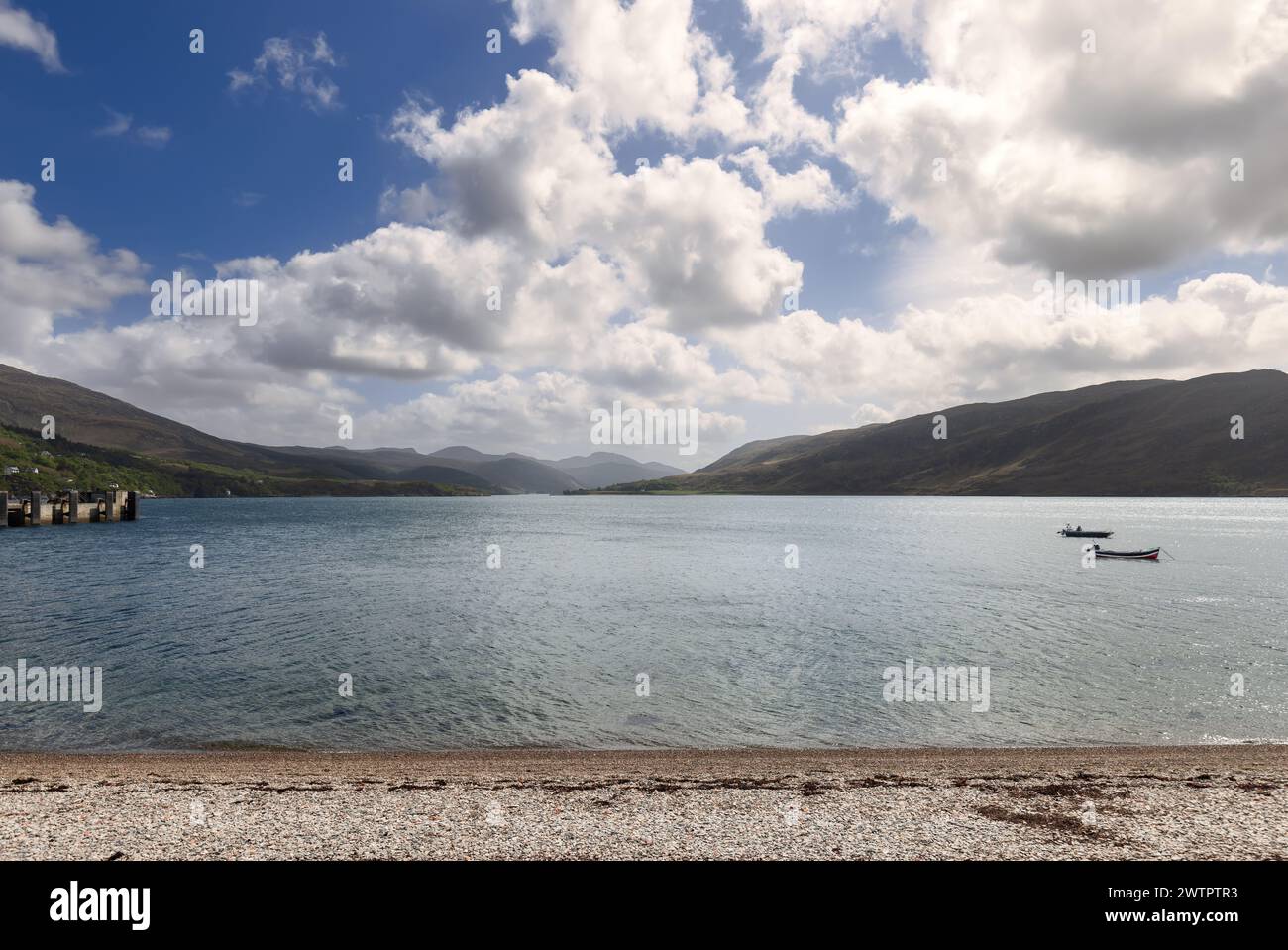 A serene Ullapool pebble beach opens to a vast loch, with a lone boats ...