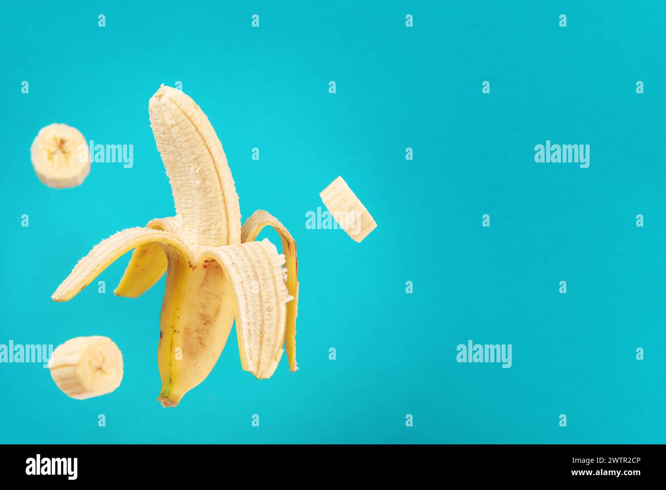 Banana floating on a blue background with the skin open and surrounded ...