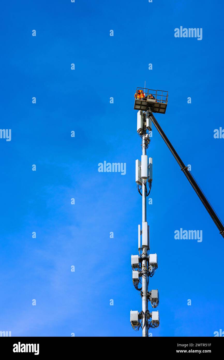 a worker repairs a cell tower while standing in a manipulator cradle ...