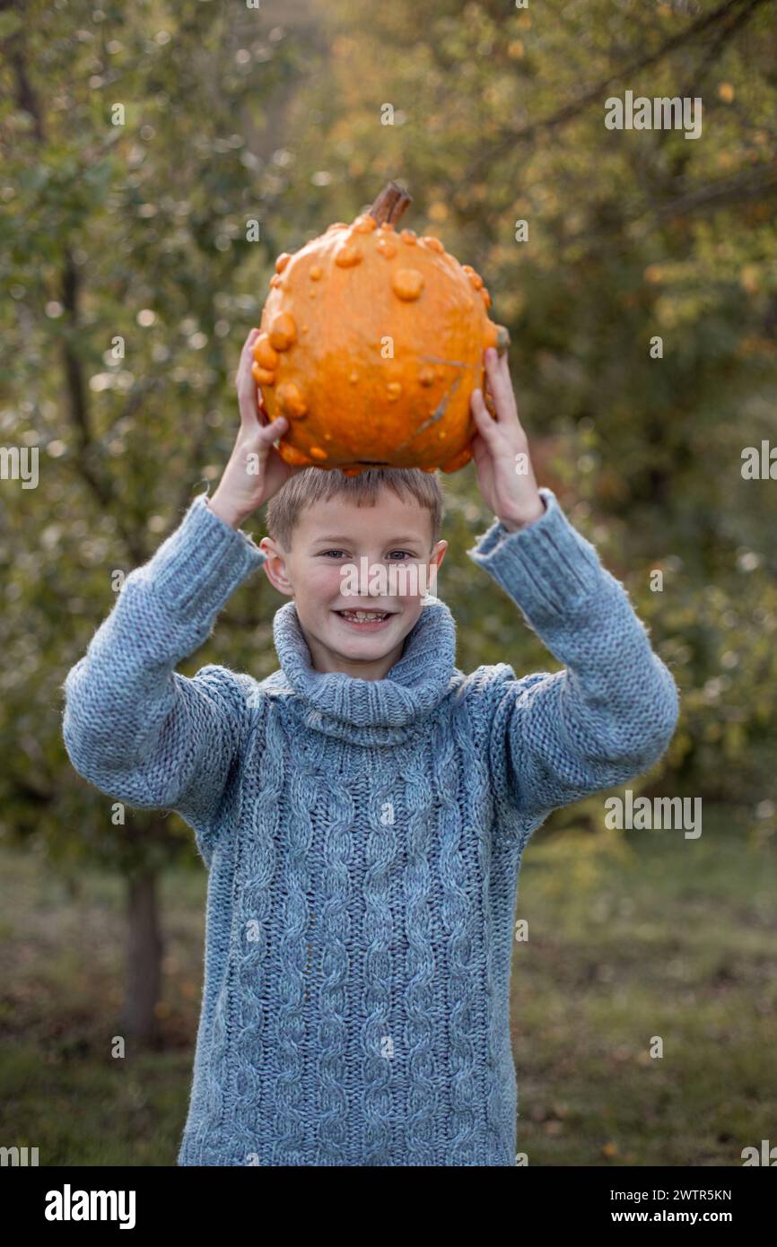 Boy in a knitted blue sweater is holding in his hands ugly orange ...