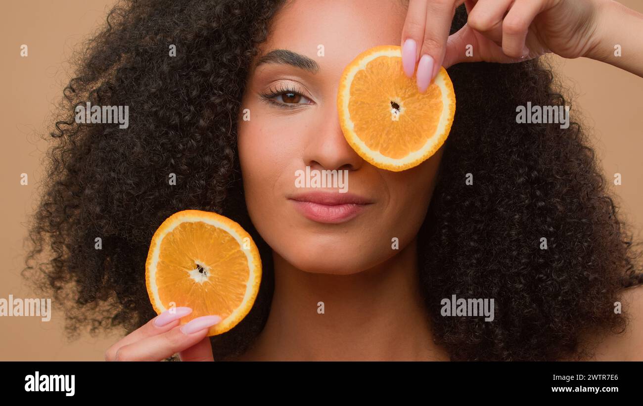 Close up ethnic model holding two slices of orange citrus posing beige ...