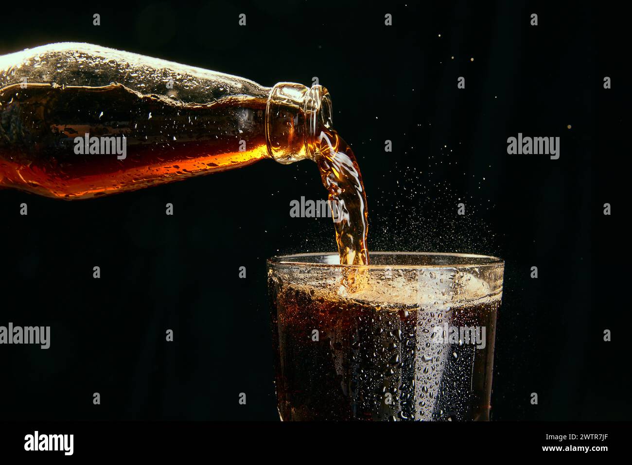 Soda, coke, dark beer pouring from bottle into glass against black ...