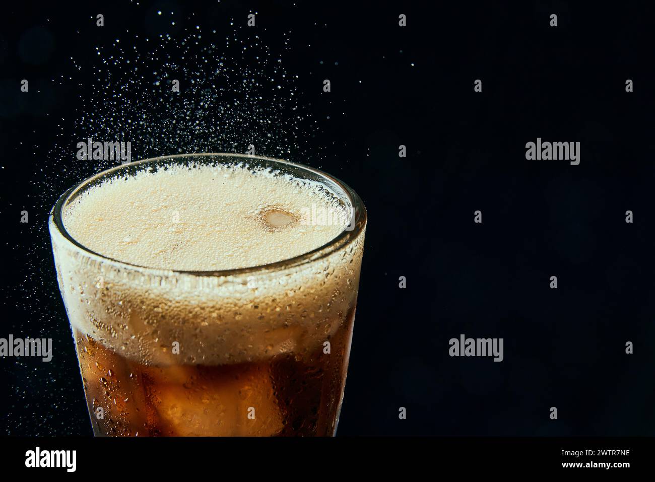 Glass wit foamy drink, soda water, coke, dark beer with ice cubes ...
