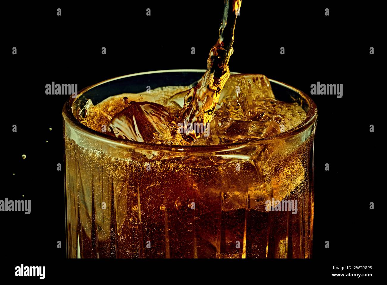 Soda, coke, dark beer pouring from bottle into glass with ice cubes against black background ...