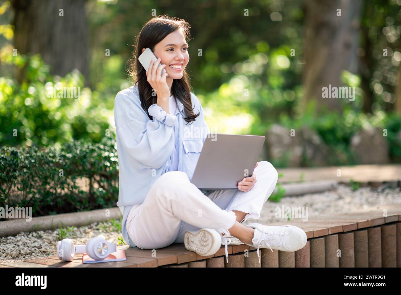Relaxed young woman engaged in a phone call while working on a laptop ...