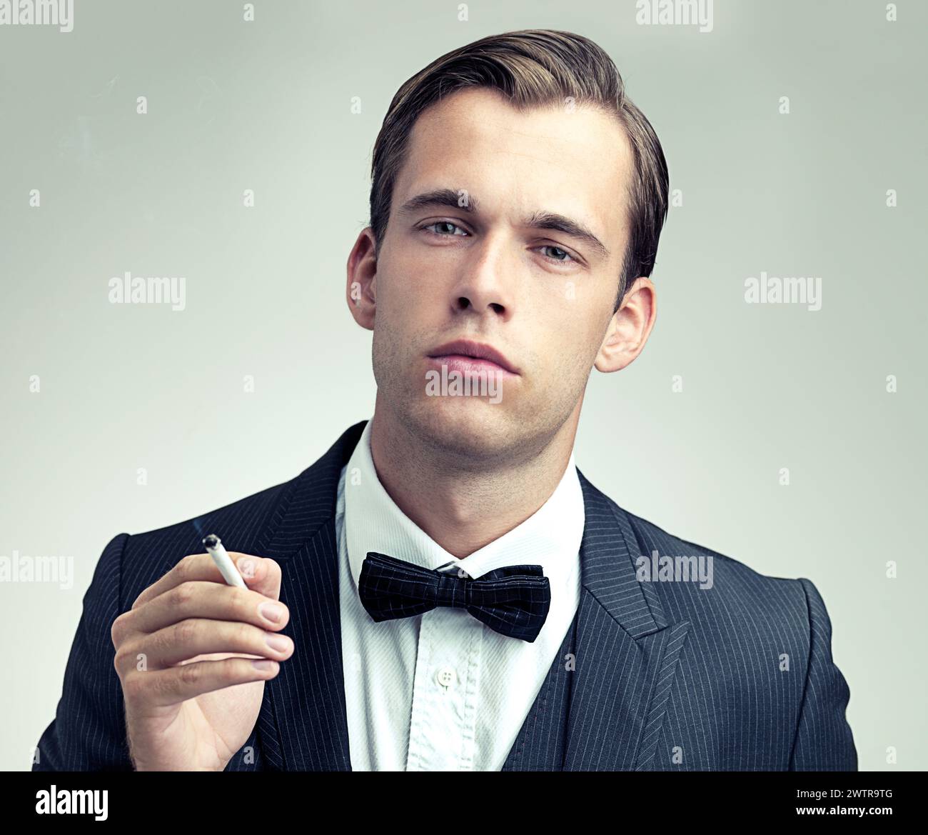 Portrait, suit or young gentleman smoking a cigarette in studio ...