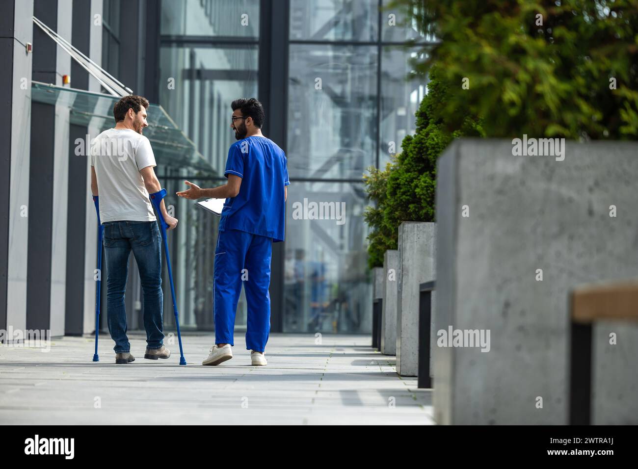 Man with crutches and a male nurse in a blue uniform walking in a ...